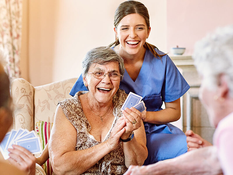 Care home carer and residents playing cards and laughing